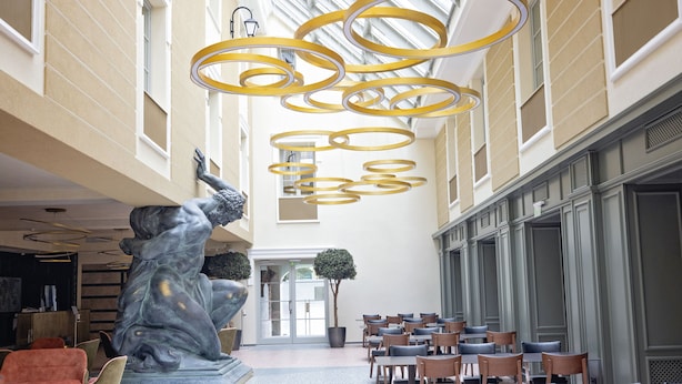 Um hall amplo com uma escultura central, diversas áreas de estar e um lustre moderno.