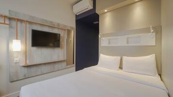 Quarto de hotel moderno com uma cama grande, televisão montada e uma estante embutida.