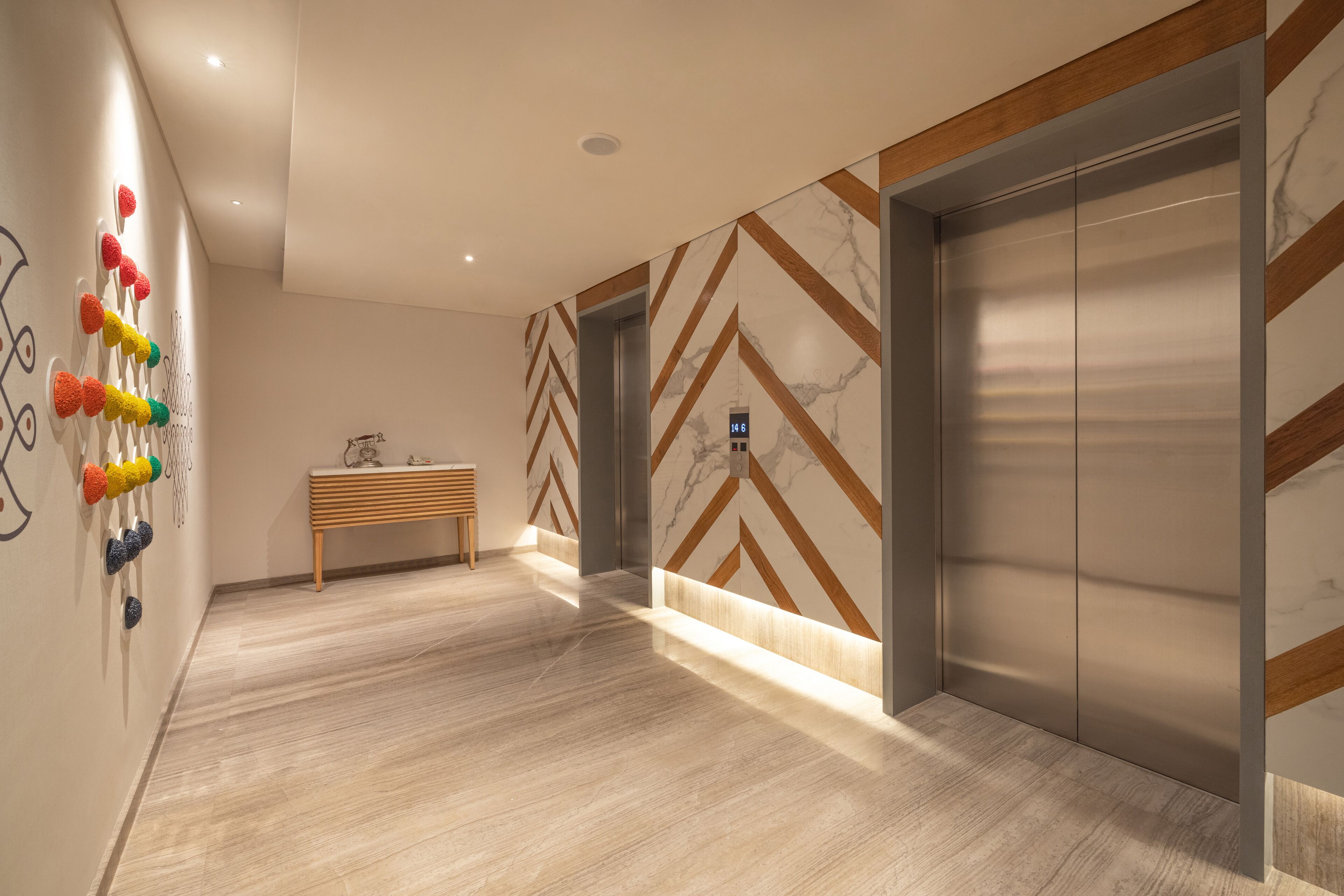Um corredor moderno com um banco de madeira, um sistema de cores fixado na parede e um elevador com padrão marmorizado.