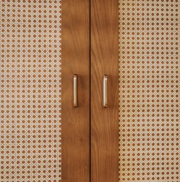 Um guarda-roupa de madeira com duas pegas e um fundo de tecido estampado.