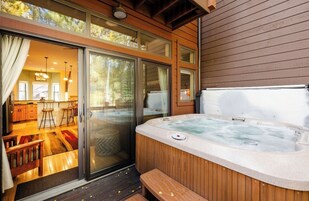 Um deck de madeira com uma banheira de hidromassagem, uma porta de vidro que dá para uma sala de jantar e vista para árvores.