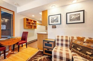 Uma sala de estar aconchegante com uma escrivaninha de madeira, uma cadeira vermelha, um sofá xadrez e duas molduras na parede.