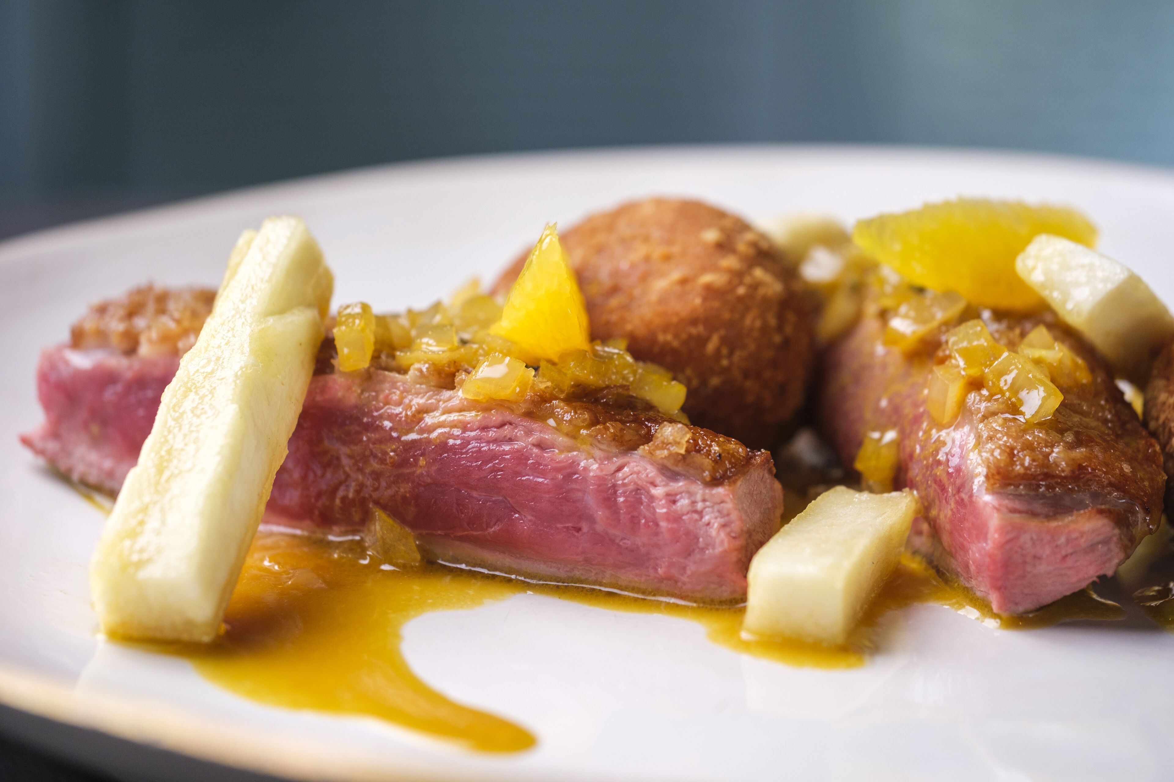Prato de comida com carne, batatas e um item redondo, possivelmente um pastel ou pão.