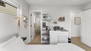 Quarto de hotel compacto com cama, pequeno espaço de cozinha e banheiro.