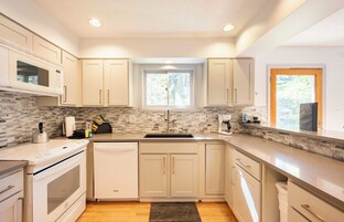 Cozinha moderna com armários brancos, painel de azulejos, forno embutido e janela que proporciona iluminação natural.