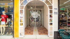 Entrada de hotel com um arco decorativo, uma loja de sapatos à direita e um manequim em exposição à esquerda.