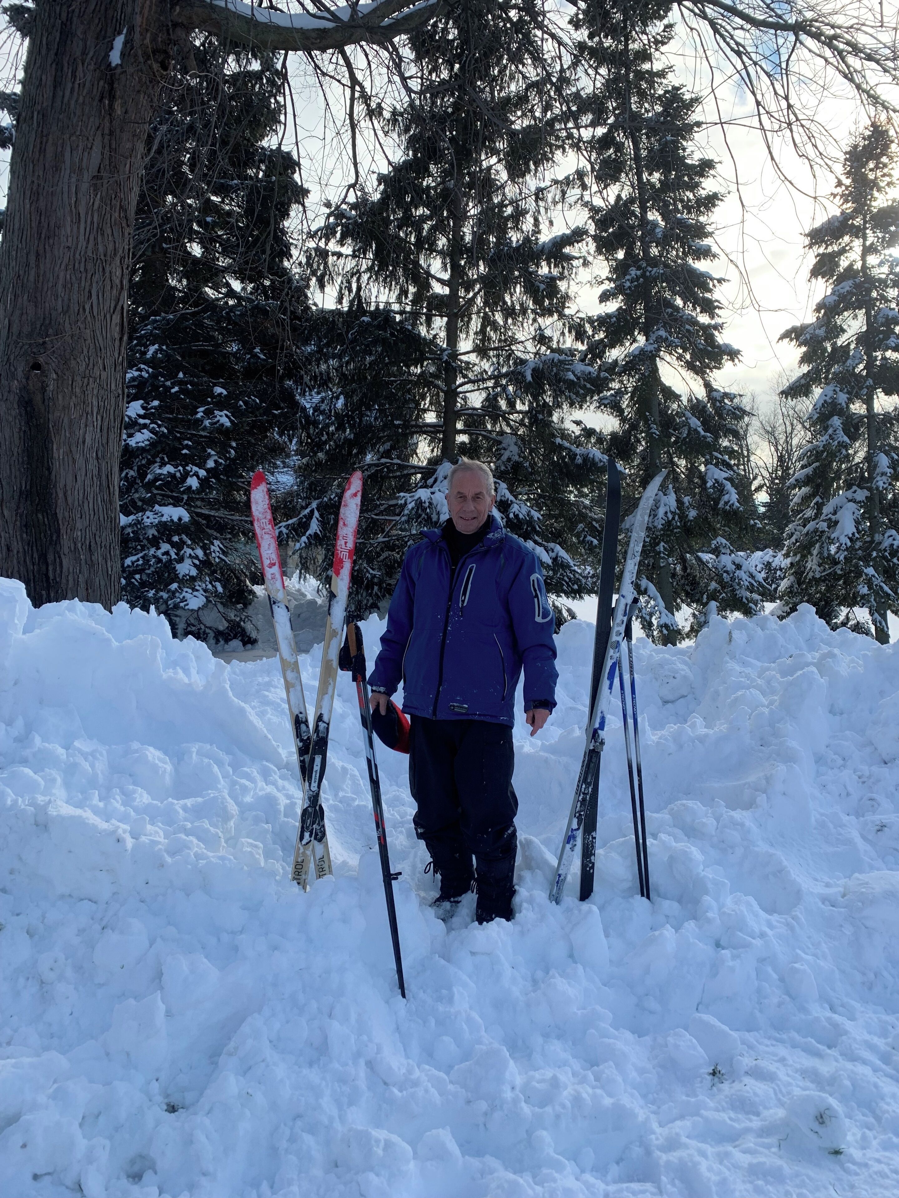 Uma pessoa em área nevada com esquis encostados numa árvore.