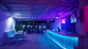 Uma área de bar com letreiro de neon, assentos e balcão.