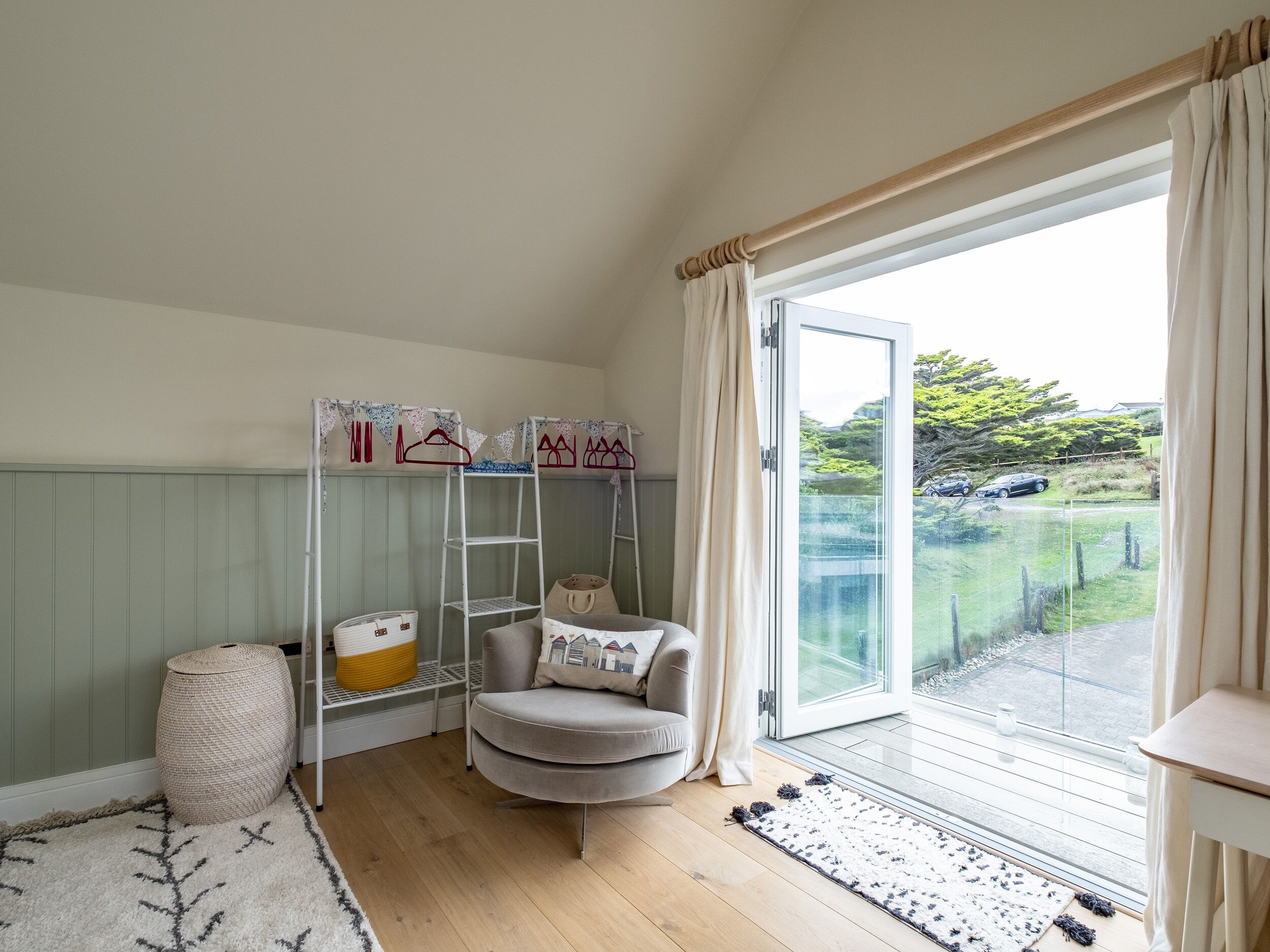 Um quarto com uma cama beliche, uma cadeira redonda pequena, uma cesta trançada e vista para uma paisagem verde através de uma porta de vidro.