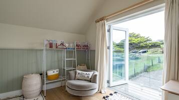Um quarto com uma cama beliche, uma cadeira redonda pequena, uma cesta trançada e vista para uma paisagem verde através de uma porta de vidro.