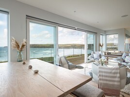 Uma sala de estar moderna com uma grande mesa de madeira, assentos confortáveis e janelas amplas com vista para o mar.