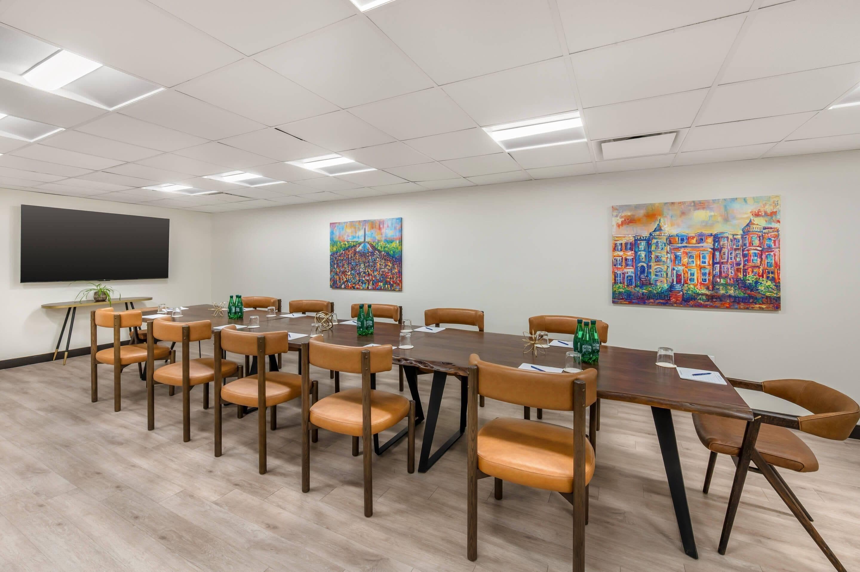 Uma sala de conferências com uma mesa comprida, cadeiras marrons e duas pinturas grandes nas paredes.
