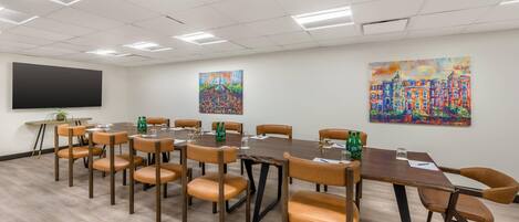 Uma sala de conferências com uma mesa comprida, cadeiras marrons e duas pinturas grandes nas paredes.