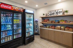 Uma área de máquinas de venda automática com refrigerantes Coca-Cola e Sprite, um letreiro com a frase 'lugar feliz' e cestos de petiscos nas prateleiras.