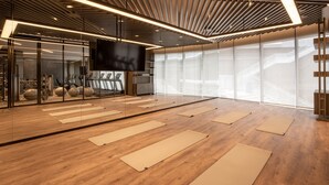 Uma academia moderna com piso de madeira, colchonetes de exercícios, um espelho grande e uma tela de televisão.