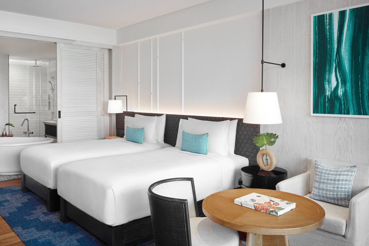 Quarto de hotel com uma cama grande, uma mesa de cabeceira, uma cadeira, uma mesa redonda pequena, um abajur e um quadro na parede.