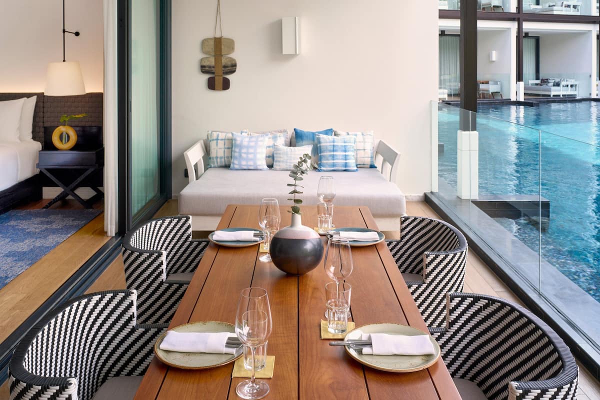 Uma sala de jantar com uma mesa de madeira posta para quatro pessoas, cercada por cadeiras listradas em preto e branco. Um vaso grande com uma planta está colocado no centro da mesa.