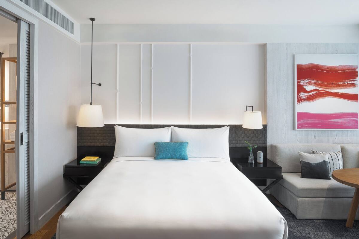 Quarto de hotel com uma cama grande, mesa de cabeceira, abajur, sofá, mesa de centro e banheiro com banheira e pia.