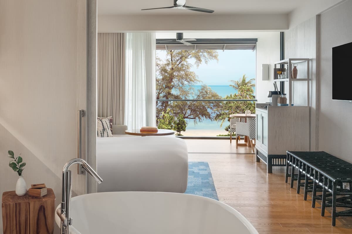 Quarto de hotel moderno com uma banheira grande, uma varanda com vista para o mar e um espaço de refeições com mesa e cadeiras.