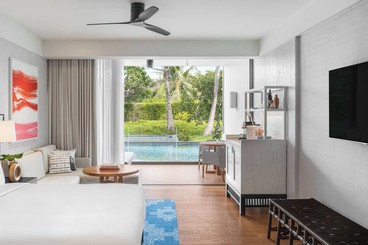Quarto de hotel moderno com uma cama grande, uma escrivaninha, televisão e varanda com vista para a piscina.