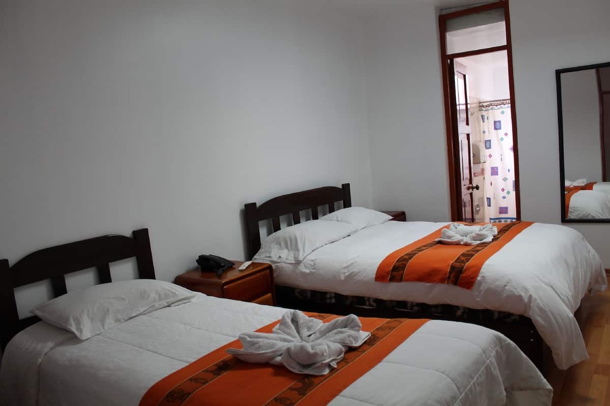 Quarto de hotel com duas camas, cada uma com roupa de cama branca e detalhes em laranja, cabeceira de madeira, mesa de cabeceira com telefone e espelho na parede.
