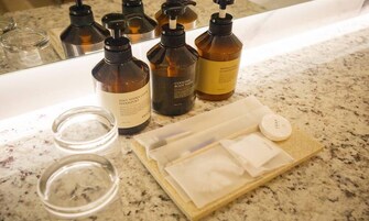 Uma bancada de banheiro com diversos produtos de higiene pessoal, incluindo garrafas de shampoo, banho e sabonete, além de uma toalha e um saboneteira.