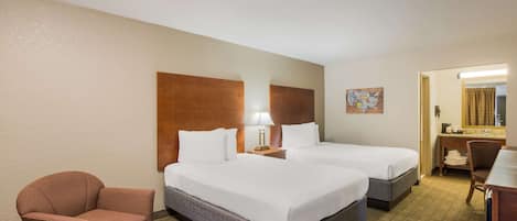 Quarto de hotel com duas camas, uma cadeira, uma escrivaninha e uma luminária.