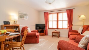 Uma sala de estar com televisão, móveis vermelhos, uma mesa de jantar com frutas e uma janela com cortinas.