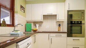 Cozinha compacta com armários brancos, lava-louças, micro-ondas e tábua de corte verde.