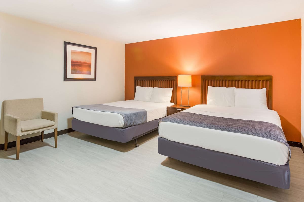 Quarto de hotel com duas camas, uma cadeira e um quadro na parede.