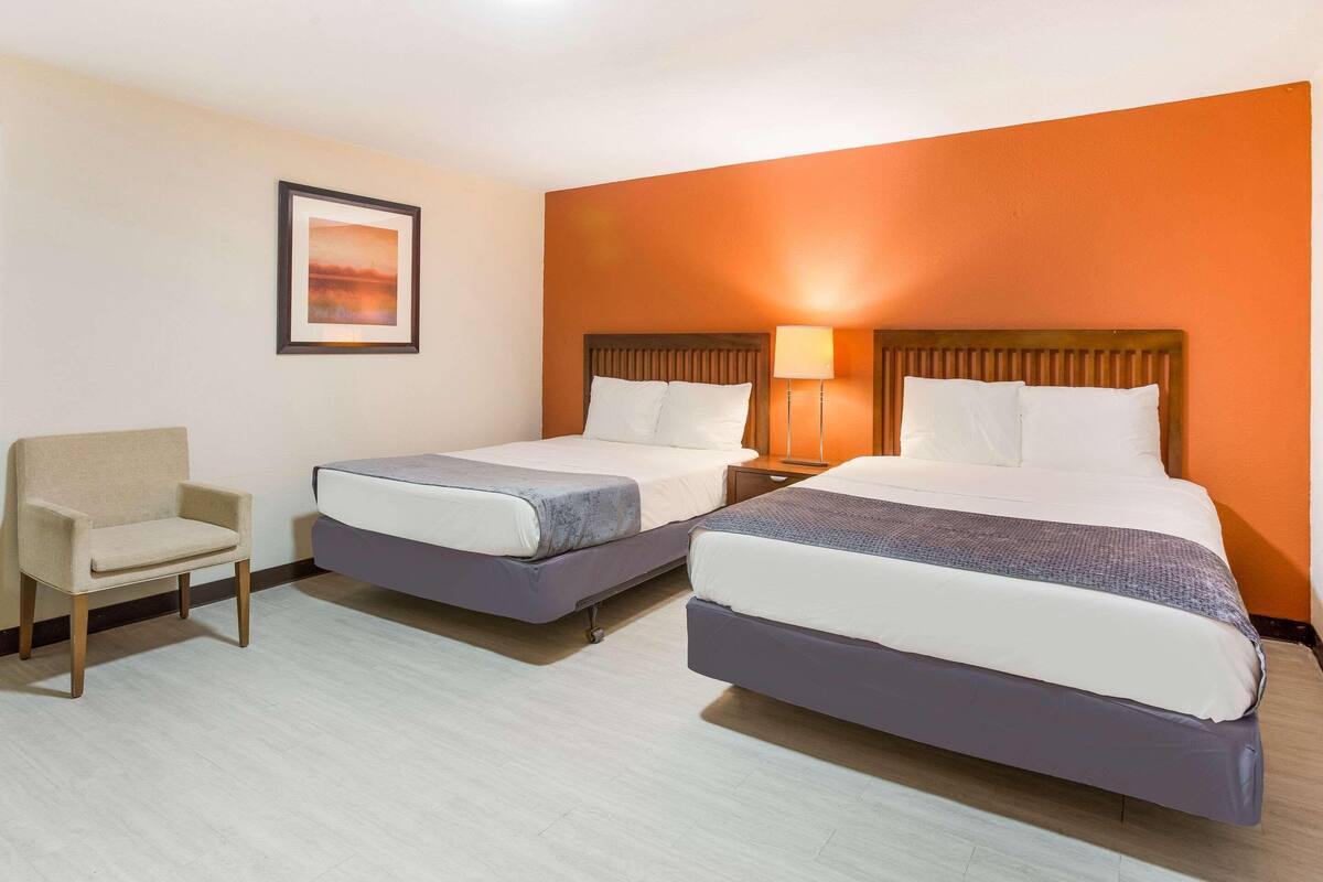 Quarto de hotel com duas camas, uma cadeira e um quadro pendurado na parede.