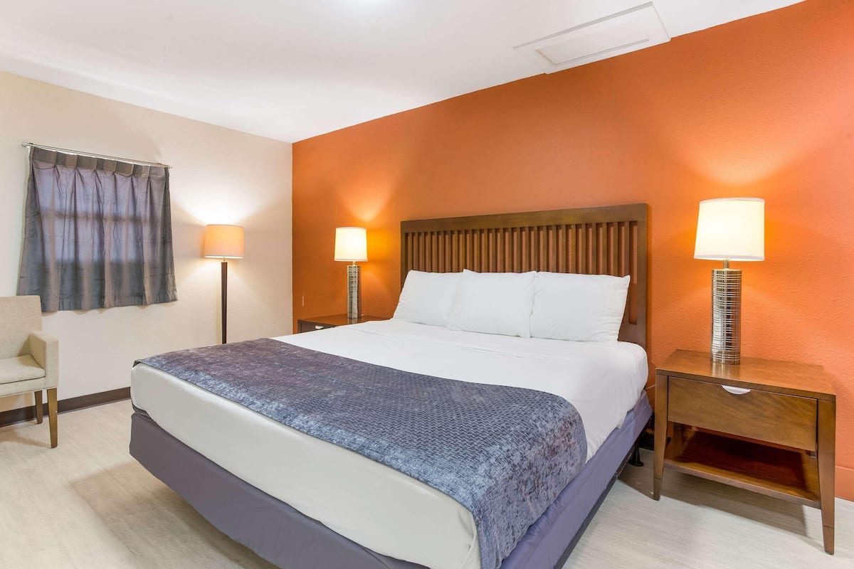 Quarto de hotel com cama, duas luminárias de cabeceira, uma cadeira e cortina.