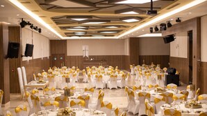 Salão de banquetes com mesas redondas dispostas para um evento formal, com toalhas brancas e fitas douradas.