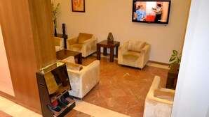 Um hall com piso de mármore, televisão na parede e vários poltronas e um sofá.