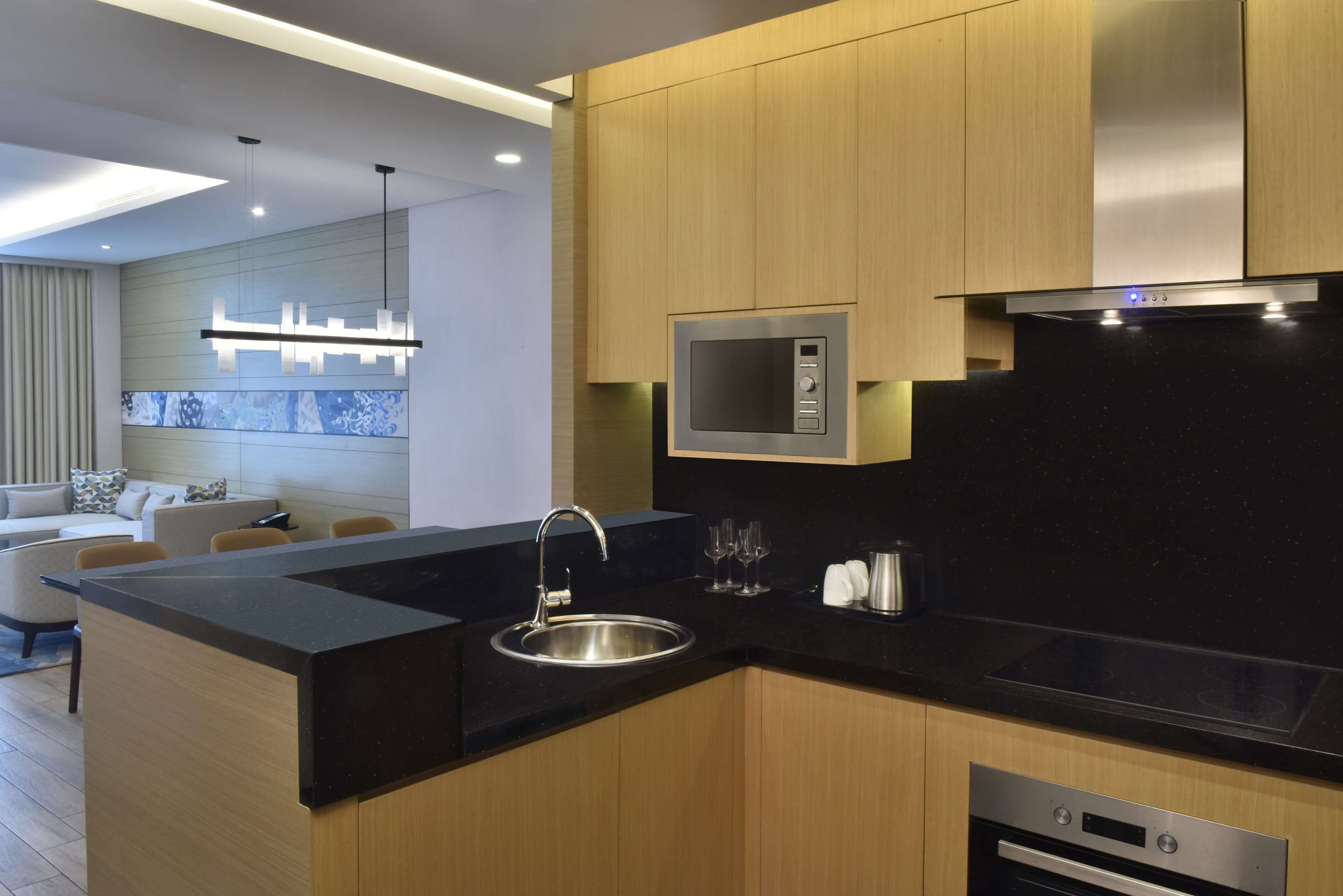 Cozinha moderna com micro-ondas embutido, pia de aço inoxidável e bancada preta.