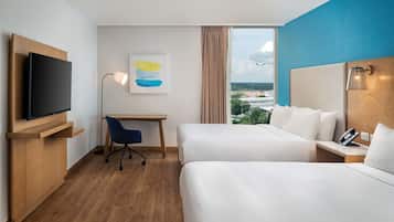 Quarto de hotel com duas camas, uma escrivaninha, uma cadeira, televisão e janela com vista para a cidade.