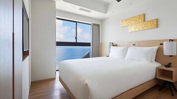 Quarto de hotel com cama grande, ventoinha no teto, vista para o mar e uma obra de arte na parede.