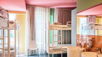 Quarto com beliche, uma cadeira, duas pias e uma janela com cortinas.