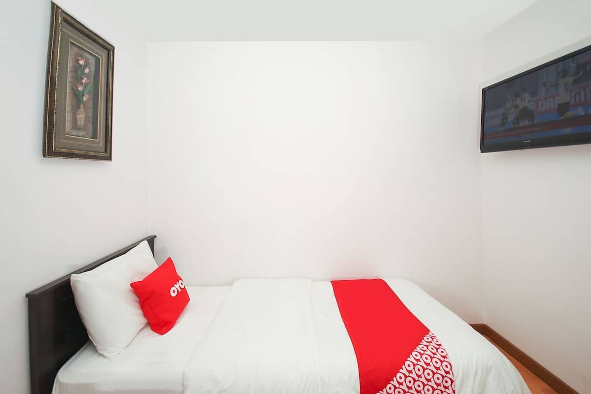 Uma cama bem arrumada com roupa de cama branca e vermelha, um travesseiro vermelho com a palavra 'oyo' e uma moldura com um quadro na parede.