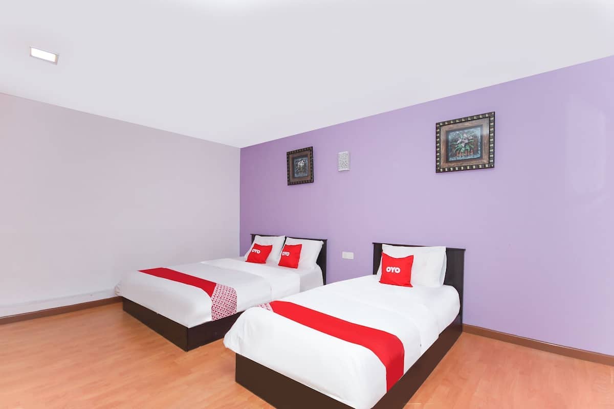 Quarto de hotel com duas camas, cada uma com roupa de cama branca e detalhes vermelhos, parede roxa e um quadro emoldurado.