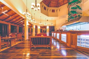 Amplo interior com piso de madeira, várias mesas de jantar e uma área de estar central com um banco.