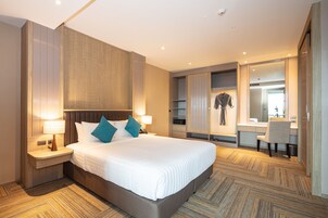 Quarto de hotel com uma cama grande, uma escrivaninha, um guarda-roupa e um espelho.