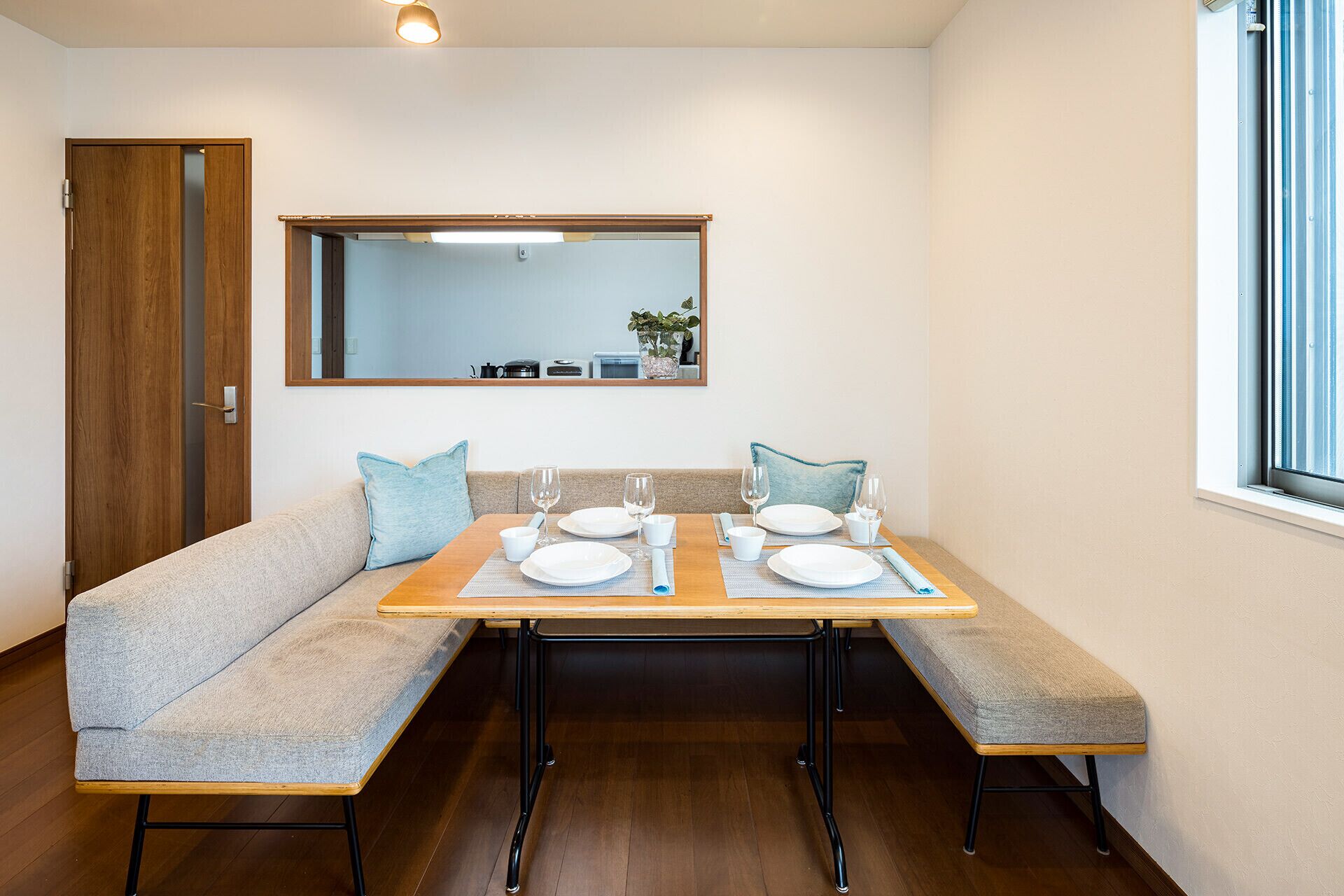 Uma área de refeições com uma mesa de madeira posta para dois, um banco e um espelho sobre a mesa.