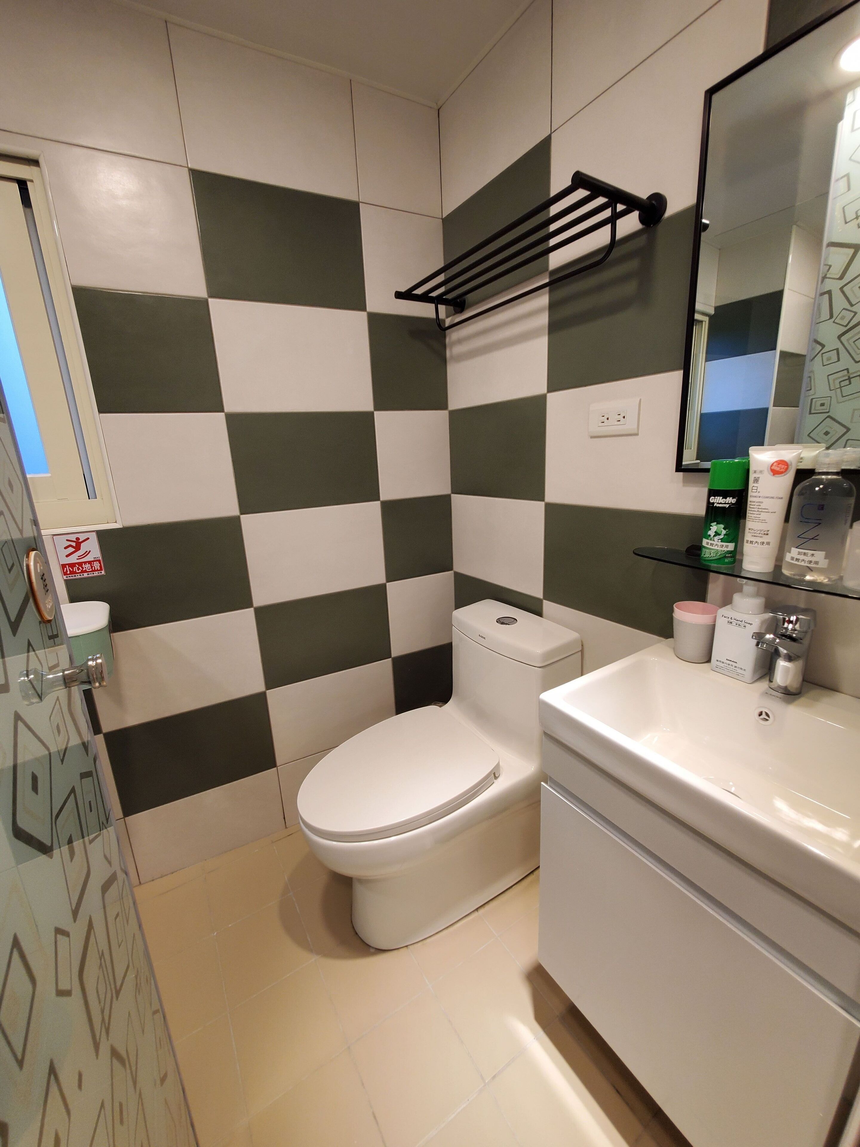 Casa de banho com sanita, lavatório e espelho. Há um porta-toalhas acima do lavatório e produtos de higiene pessoal no balcão.