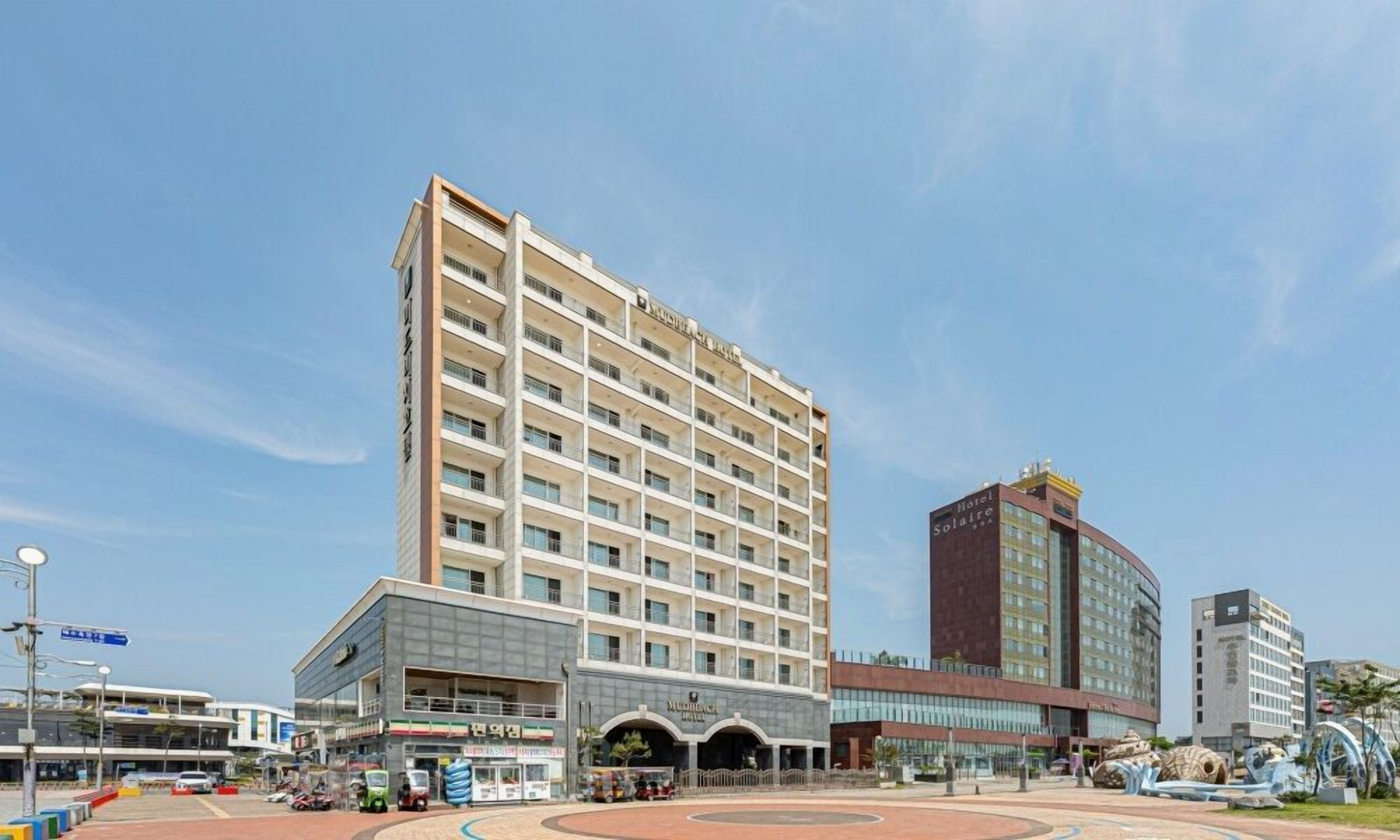 Hotel de vários andares com design moderno, destacando uma entrada imponente e área de estacionamento na frente.