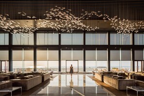 Um hall espaçoso com teto alto, grandes janelas e vista para o mar.