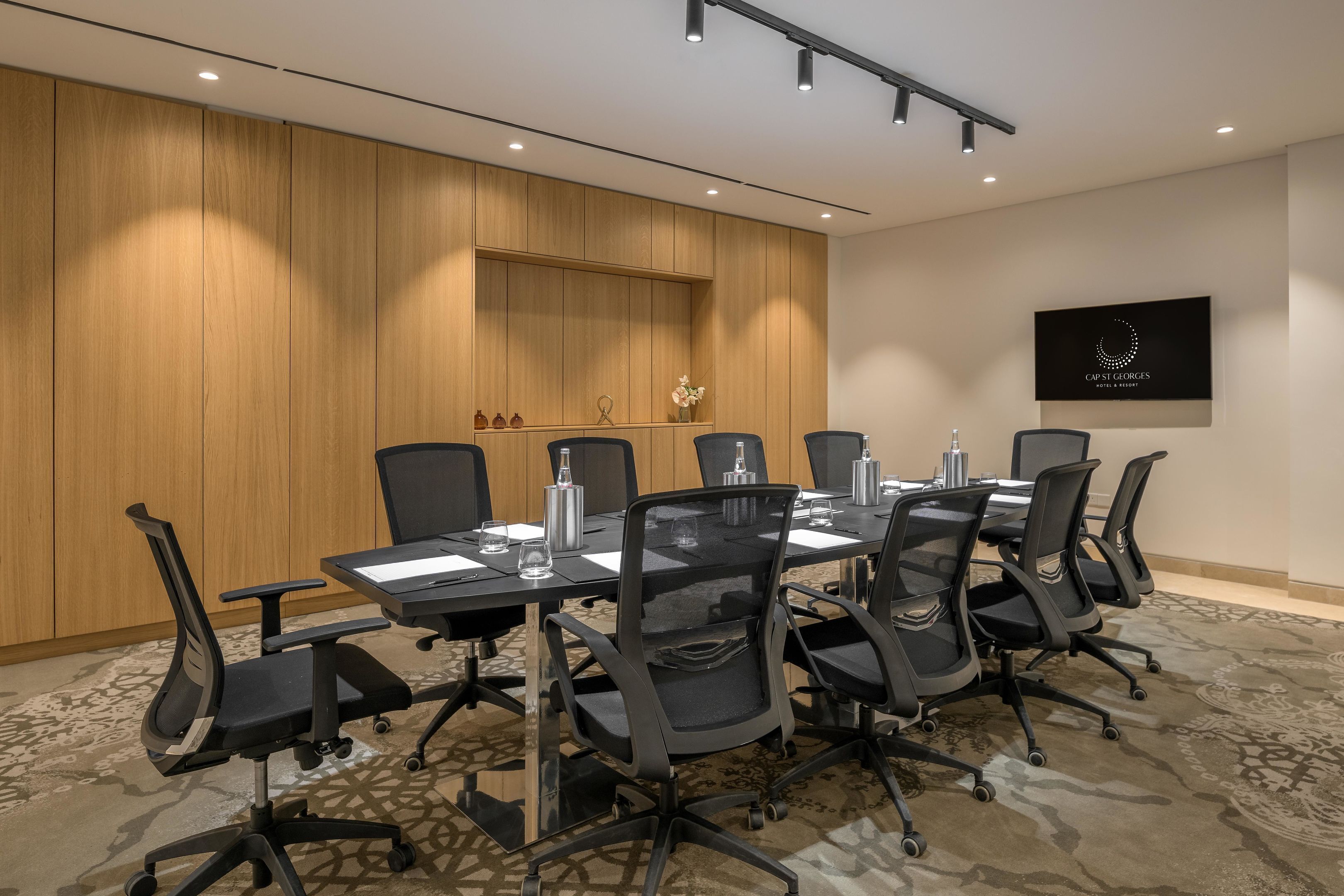 Uma sala de conferências com uma mesa comprida, cadeiras pretas e um painel de parede de madeira.