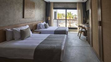 Quarto de hotel com duas camas, uma escrivaninha, uma cadeira, televisão e varanda com vista para palmeiras.