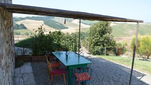 Mesa e cadeiras montadas num pátio de cascalho com vista para colinas e árvores.