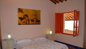 Quarto com cama, mesas de cabeceira, um quadro e janela com persiana aberta.